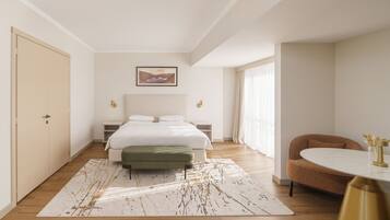Quarto com cama, mesas de cabeceira, um banco verde, uma mesa redonda e uma cadeira.