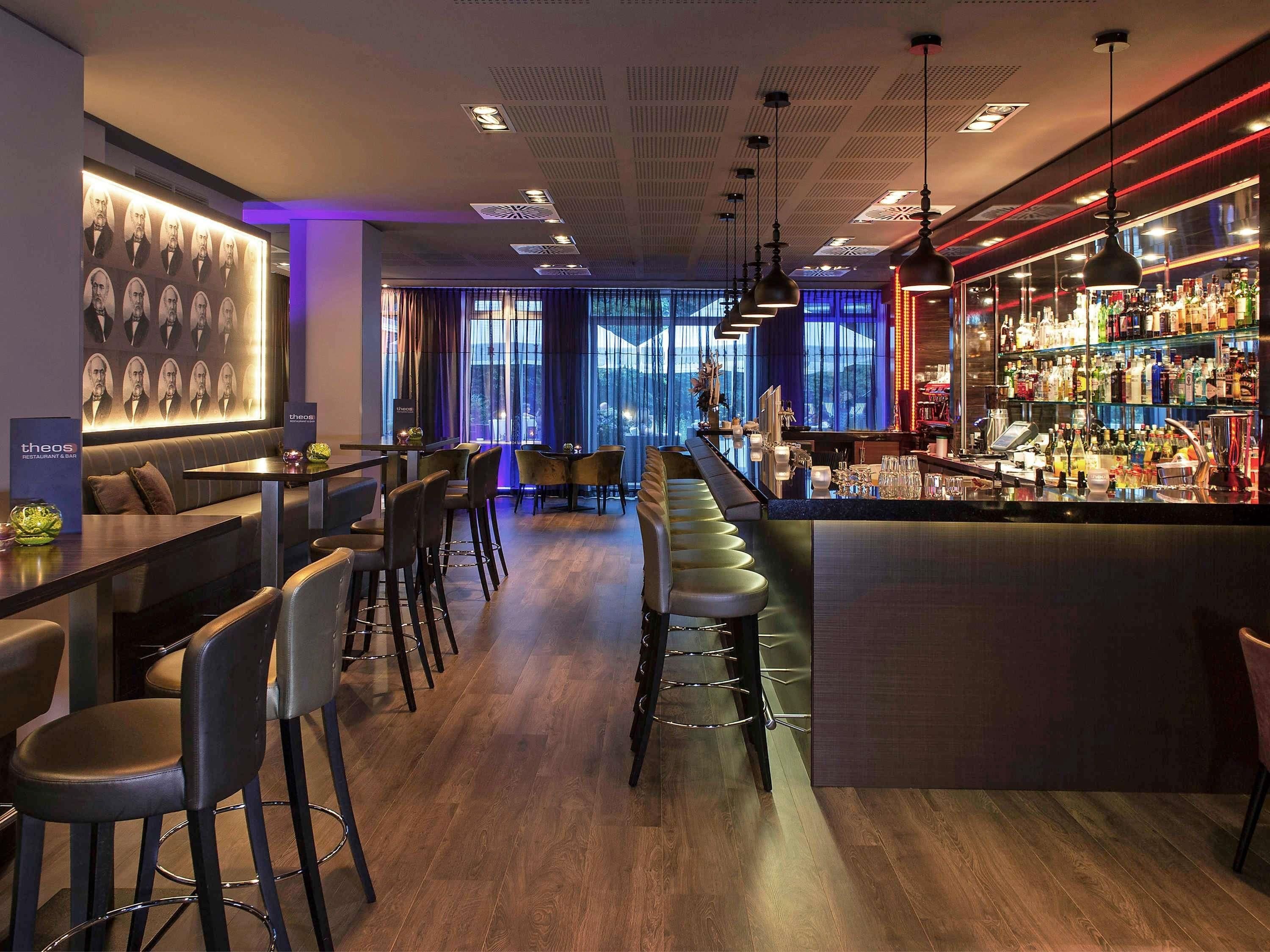 Uma área de bar moderna com um balcão comprido, banquetes e um espaço de estar com um sofá e cadeiras.