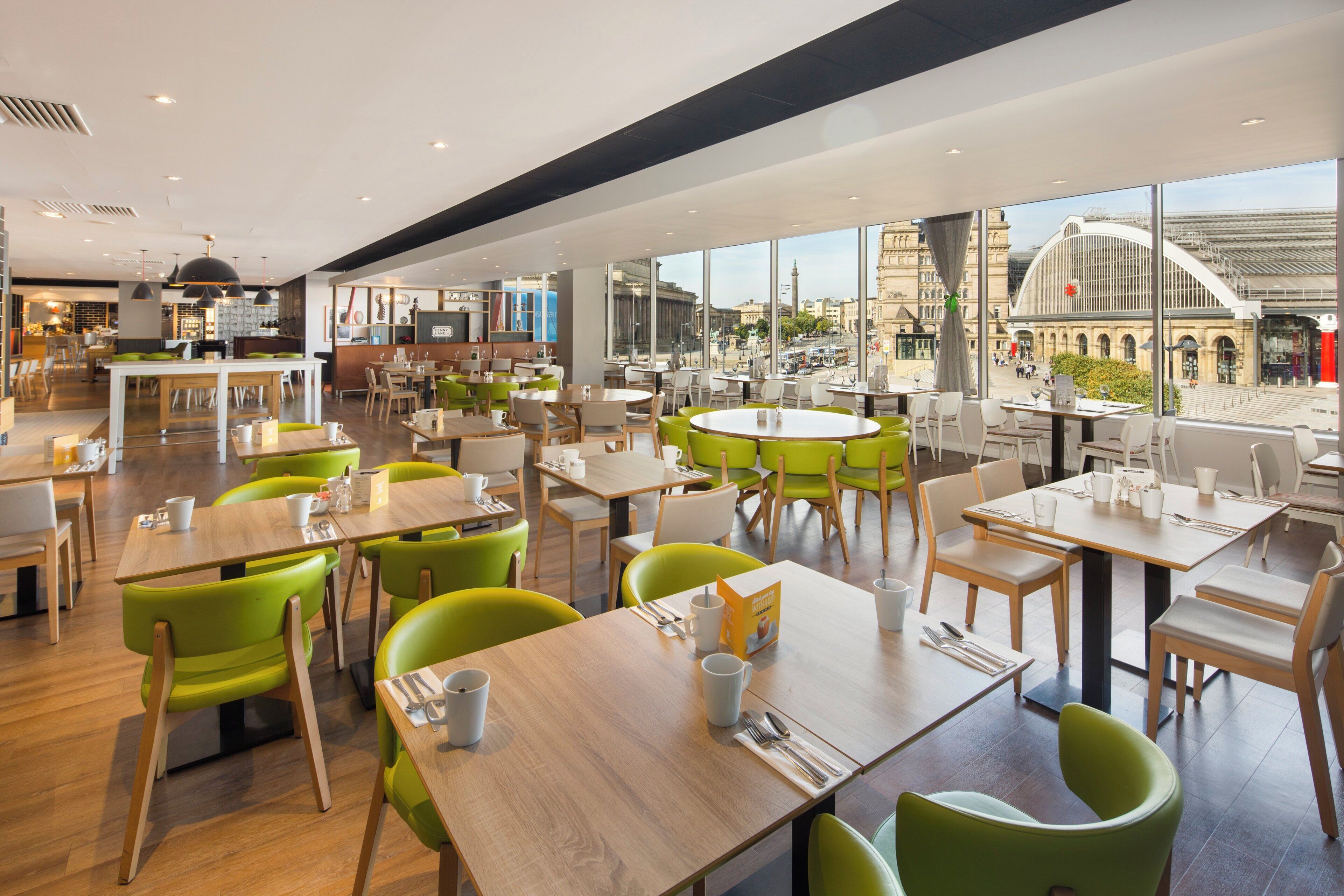 Um restaurante moderno com várias áreas de estar, grandes janelas com vista para a cidade e diferentes estilos de mesas e cadeiras.