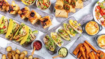 Diversos pratos, incluindo tacos, burritos, frango grelhado e batatas assadas, indicando uma variedade de opções para a refeição.