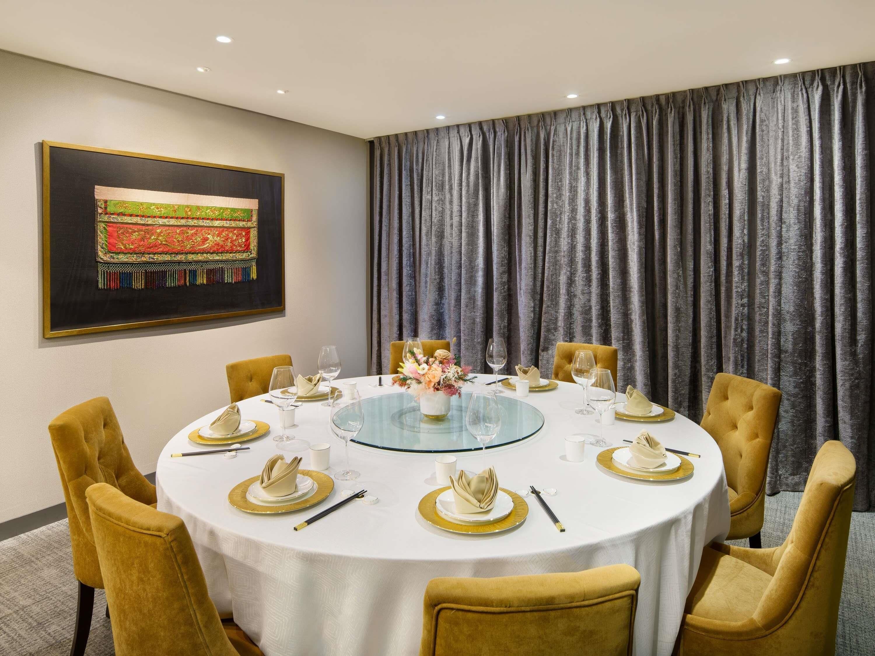 Uma mesa de jantar redonda com detalhes dourados, cercada por cadeiras de veludo, posta para uma refeição.