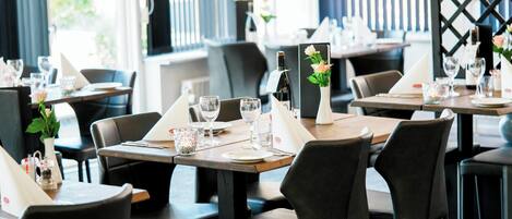 Um restaurante com mesas postas para refeições, apresentando um interior moderno com cadeiras escuras e uma mesa de madeira.