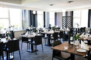 Uma sala de jantar com várias mesas preparadas para servir, com cadeiras pretas e piso coberto por carpete.