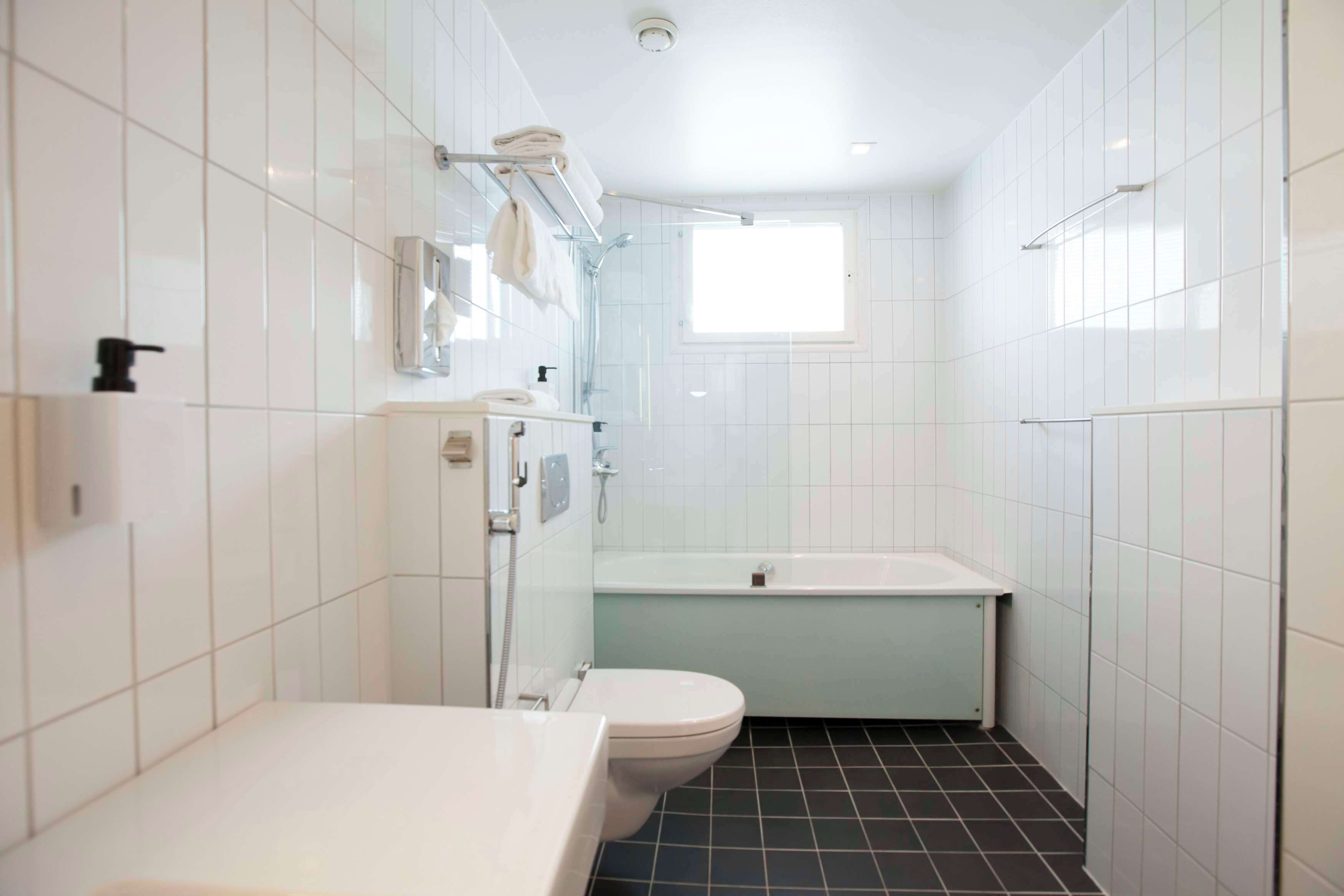 Uma casa de banho compacta com azulejos brancos, sanita branca, lavatório branco e banheira branca.