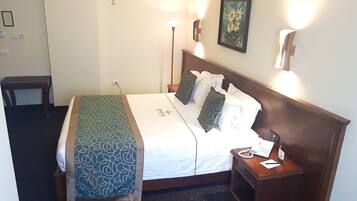 Quarto de hotel com cama bem arrumada, mesa de cabeceira com telefone e luminárias fixadas na parede.