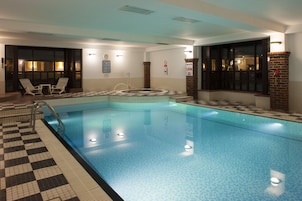 Piscina com piso quadriculado, cadeiras de sol e um pilar de tijolos.