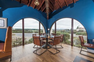 Uma sala de jantar com uma mesa redonda e cadeiras, janelas arqueadas amplas e vista para o campo.