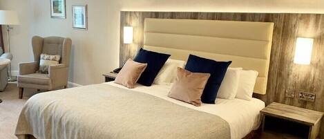 Quarto de hotel com cama grande, duas mesas de cabeceira, uma cadeira e uma luminária.