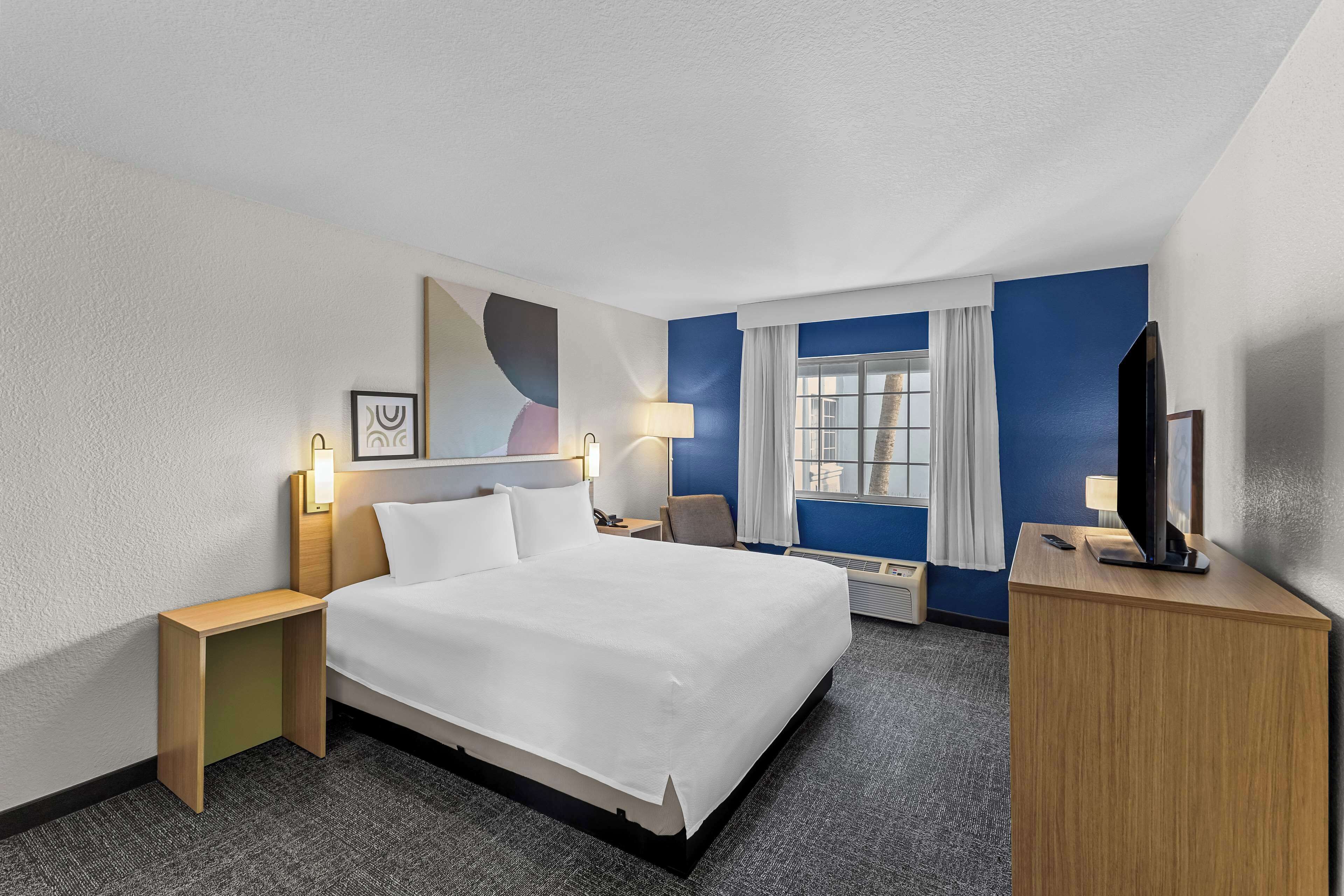 Quarto de hotel com cama grande, mesas de cabeceira, escrivaninha com televisão e janela com cortinas.