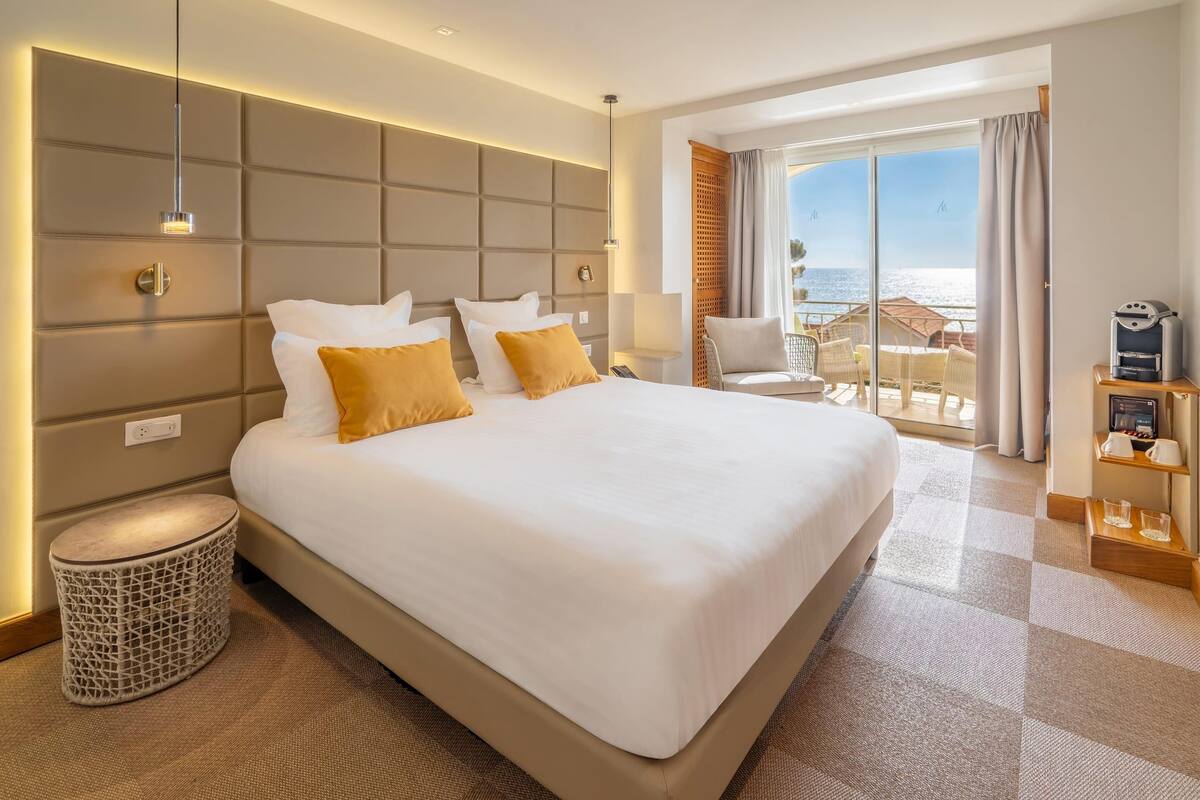 Quarto de hotel com cama grande, vista para o mar, varanda com área de estar externa e design moderno.