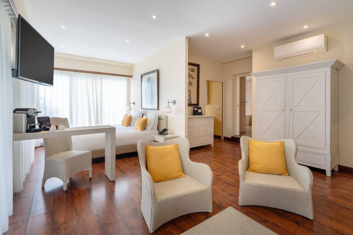 Quarto de hotel com cama, duas poltronas, escrivaninha, televisão e guarda-roupa.