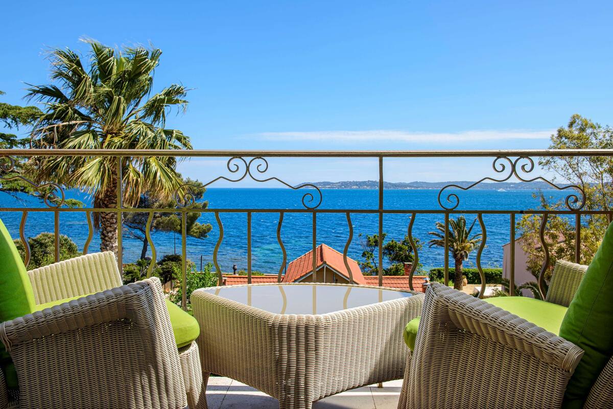 Varanda com móveis de vime e vista para o mar.