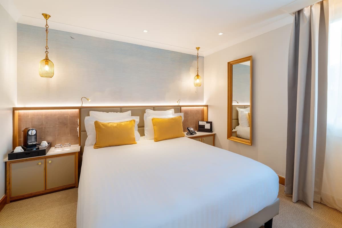 Quarto de hotel com uma cama grande, mesas de cabeceira, um espelho e um lustre.
