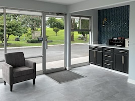 Um interior moderno com porta de vidro deslizante para um jardim, uma poltrona cinza e uma cozinha preta com ladrilhos backsplash em padrão herringbone.
