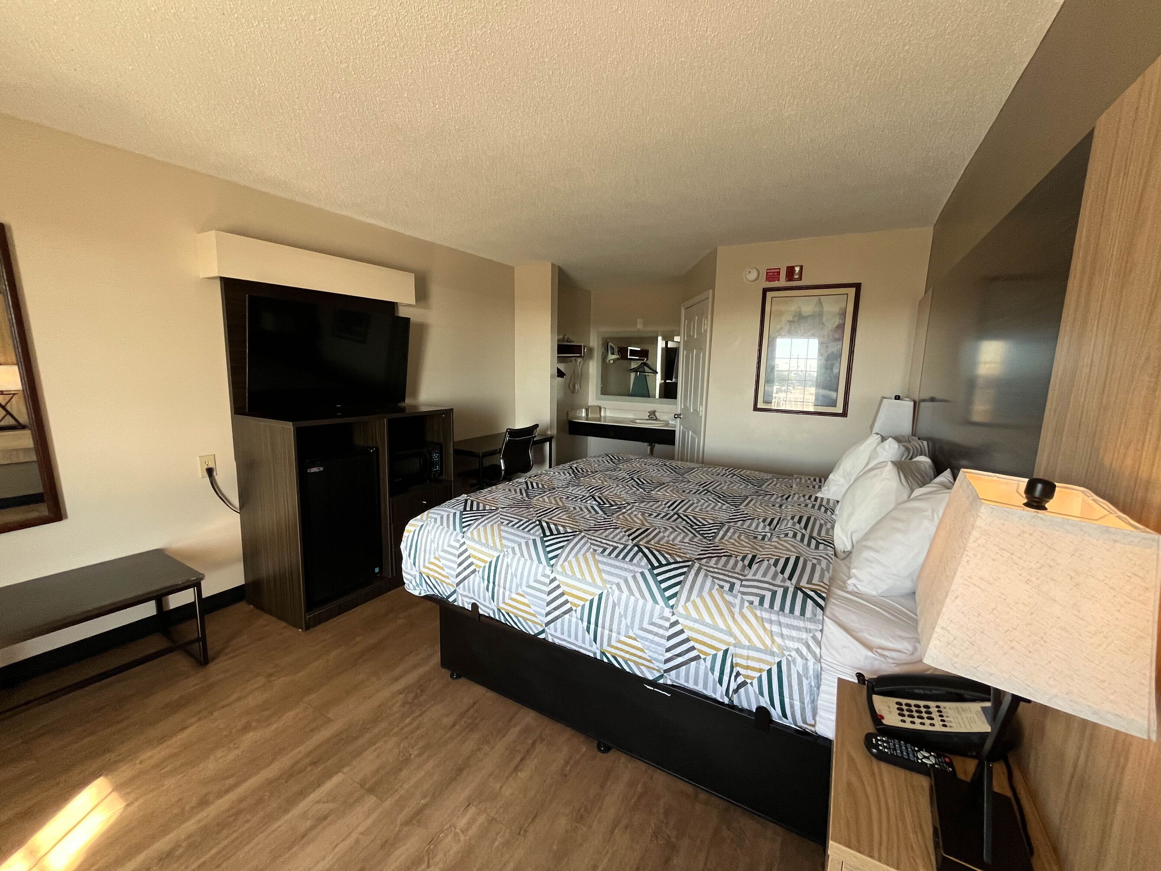 Quarto de hotel com cama, televisão, escrivaninha, espelho e banheiro.