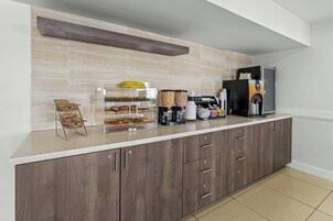 Uma cozinha com bancada, cafeteira, frigorífico e uma prateleira com petiscos.