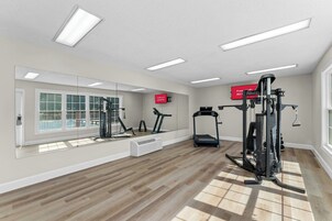Uma academia com equipamentos de exercícios, um espelho grande e vista para uma piscina.