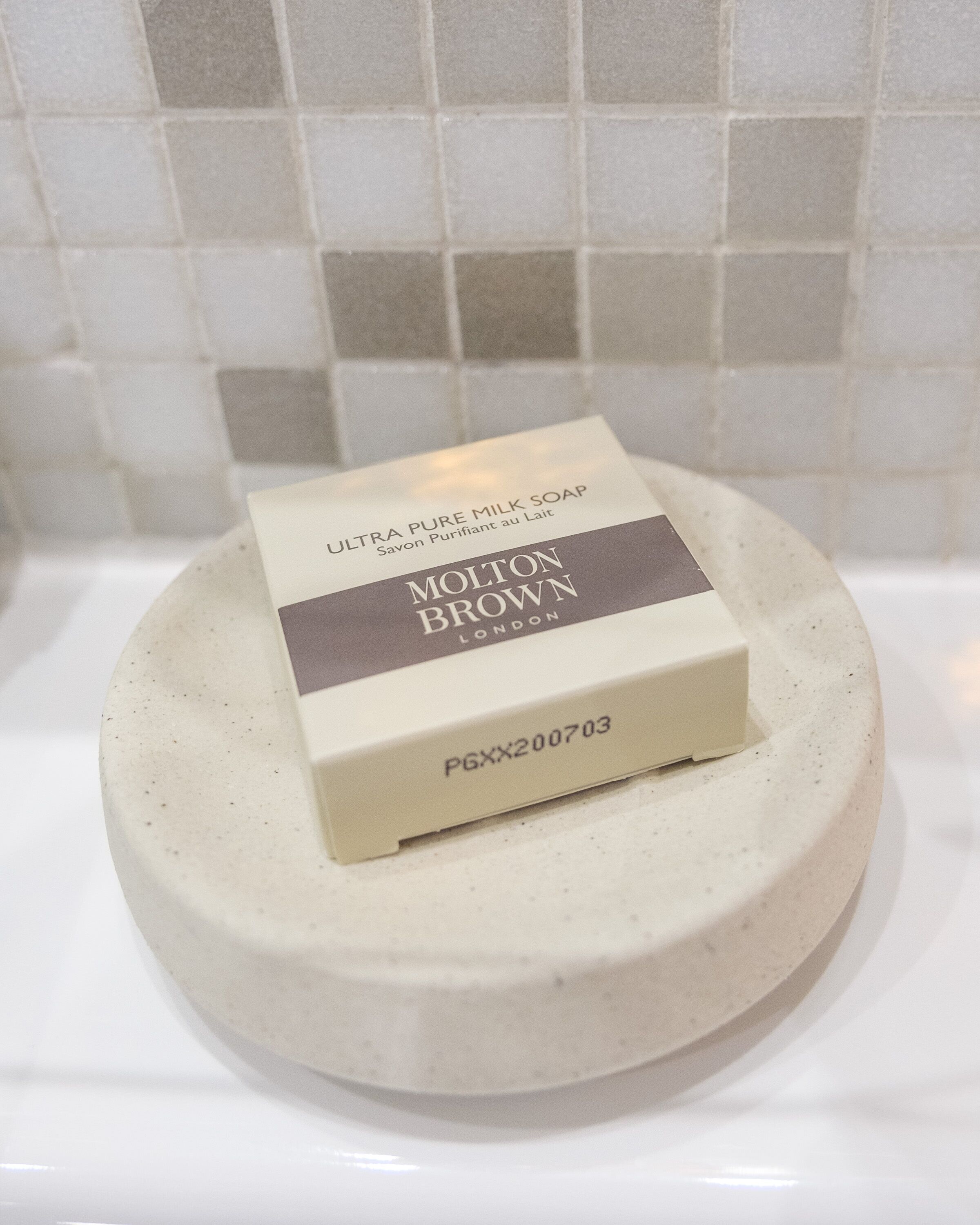 Uma barra de sabonete Molton Brown sobre um porta-sabonete de cerâmica branca.
