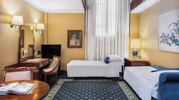 Quarto de hotel com duas camas, uma mesa, uma cadeira, televisão e uma janela grande com cortinas.