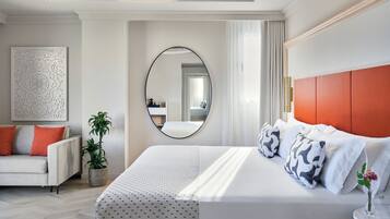 Quarto de hotel moderno com uma cama grande, um sofá, um vaso de plantas e um espelho.