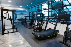 Uma academia com equipamentos de ginástica, janelas amplas e uma parede azul.