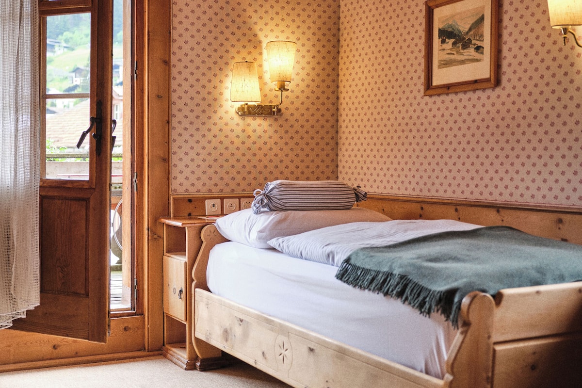 Quarto de madeira com uma cama, janela e luminária fixada na parede.