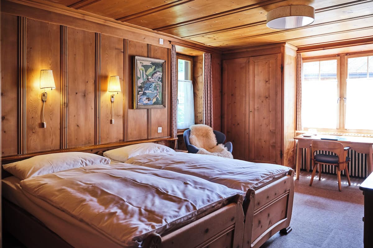 Quarto com painéis de madeira, duas camas, uma escrivaninha e uma cadeira.