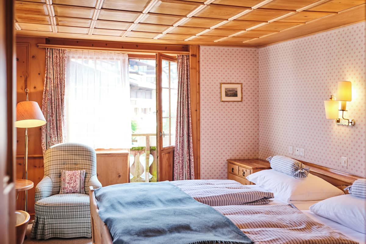 Um quarto aconchegante com uma cama, uma cadeira, uma mesinha e uma janela com cortinas.