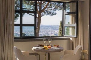 Mesa de jantar com vista panorâmica através de grandes janelas, duas taças de vinho branco e uma refeição.