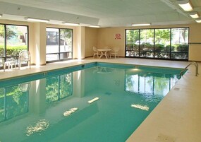 Piscina interna com água cristalina, cercada por janelas e uma mesa com cadeiras.