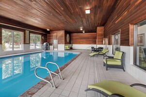 Uma área de piscina com teto de madeira, chão ladrilhado e espreguiçadeiras.