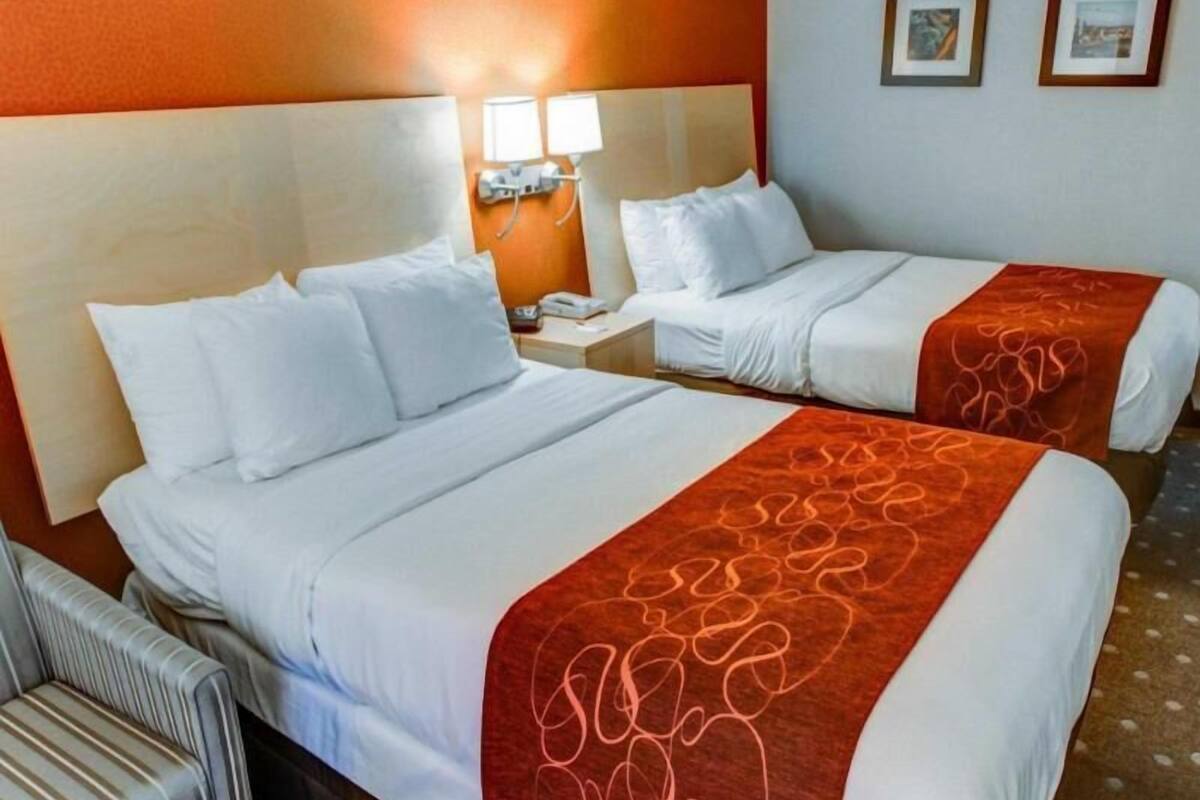 Quarto de hotel com duas camas, uma mesa de cabeceira, uma luminária e uma cadeira.