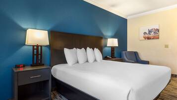 Quarto de hotel com uma cama grande, duas mesas de cabeceira com luminárias, uma cadeira e um quadro na parede.