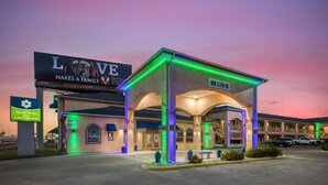 Um hotel com um letreiro 'LOVE MAKES A FAMILY', uma área externa coberta e um estacionamento.