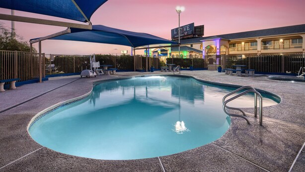 Uma piscina com área coberta, cerca e um edifício com placa ao fundo.