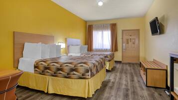 Quarto de hotel com duas camas, uma escrivaninha, uma cadeira, uma televisão e uma porta.