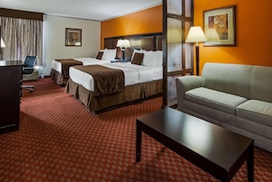 Quarto de hotel com duas camas, um sofá, uma escrivaninha e um abajur.