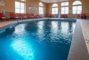 Piscina interior com espreguiçadeiras vermelhas e um deck ladrilhado.