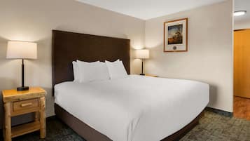 Quarto de hotel com uma cama grande, duas mesas de cabeceira com luminárias, uma mesinha de cabeceira de madeira, um quadro na parede e piso coberto por carpete.