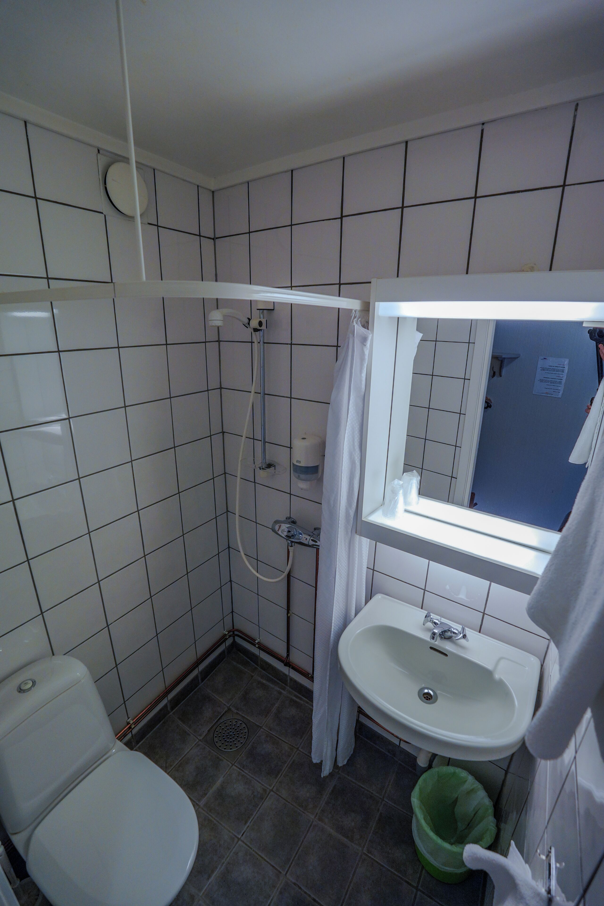 Um banheiro pequeno com revestimento de azulejos, vaso sanitário, pia e chuveiro.