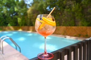 Um copo com bebida rosa, uma fatia de laranja e um canudo, apoiado em um corrimão de piscina.