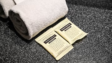 Uma toalha enrolada e dois pacotes de Verheesia Facial Bar sobre uma superfície texturizada.