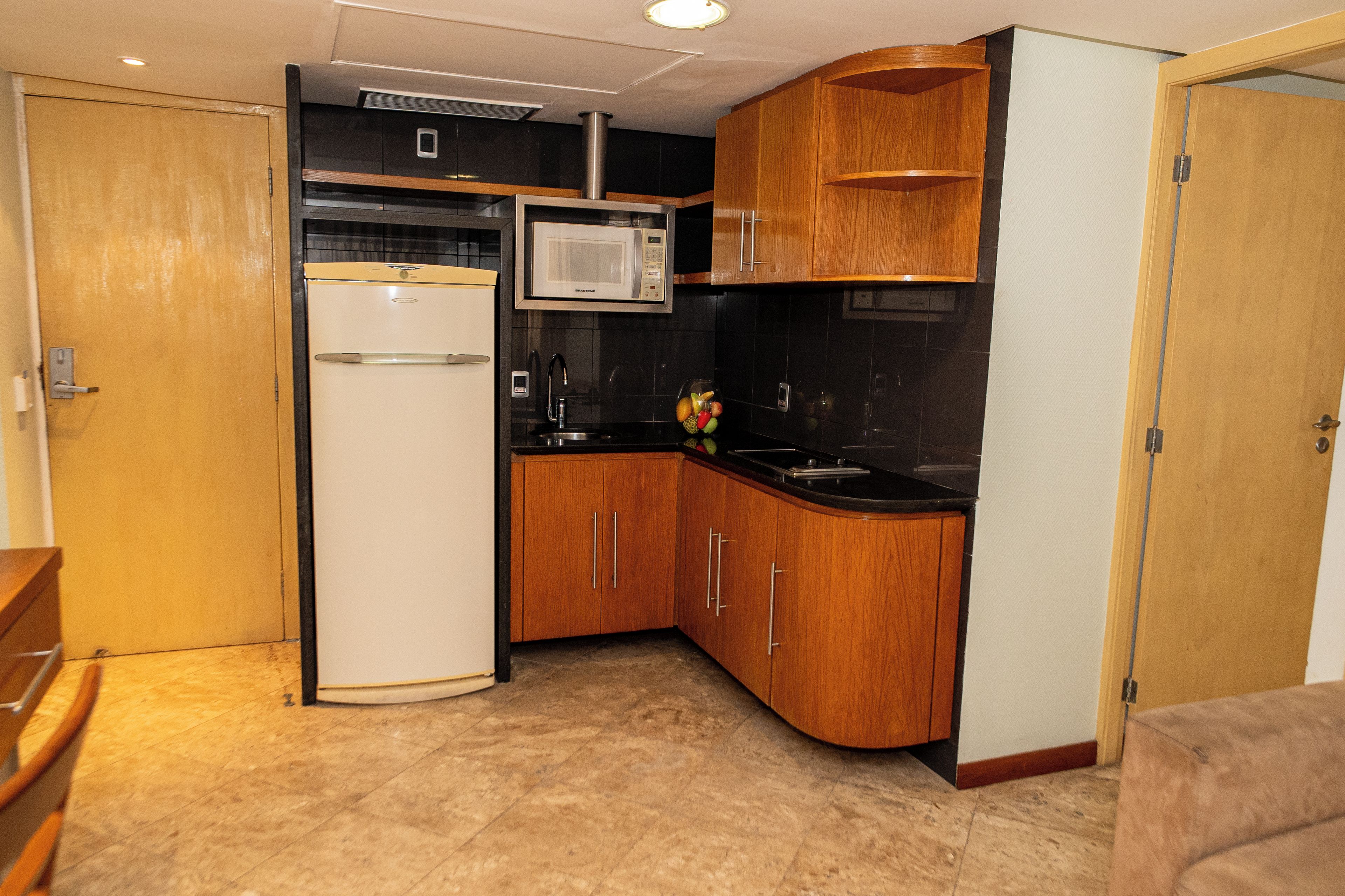 Cozinha compacta com geladeira, micro-ondas e armários de madeira.