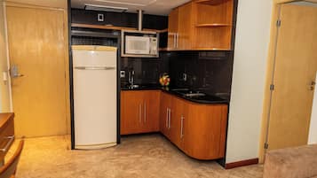 Cozinha compacta com geladeira, micro-ondas e armários de madeira.