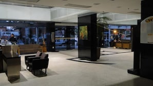 Um hall amplo com móveis modernos, um balcão de recepção e uma tela grande exibindo uma imagem.