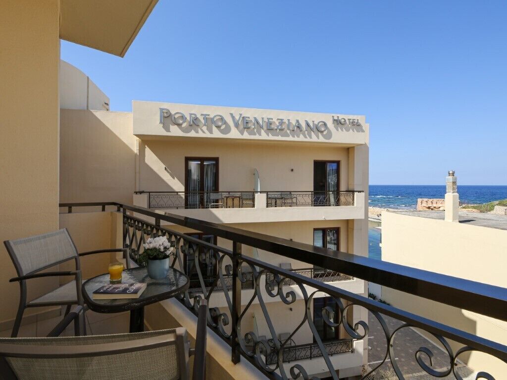 Uma varanda de hotel com vista para o mar, uma mesa com uma cadeira e um vaso de planta.