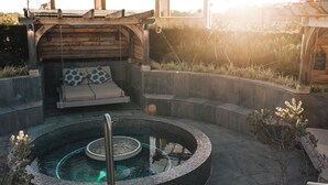 Uma banheira de hidromassagem com deck de madeira e área de estar, cercada por paredes de pedra e plantas.
