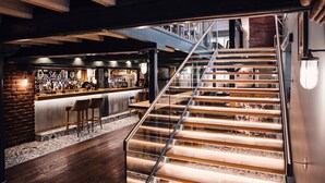 Uma área de bar com balcão e banquetas, uma escadaria com guarda-corpo de vidro e um piso estampado.