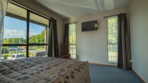 Quarto de hotel com uma cama grande, televisão na parede e vista para o exterior através de amplas janelas.