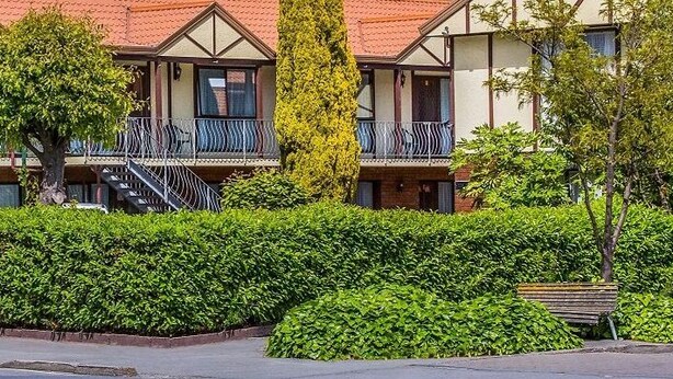Um hotel de dois andares com telhado de telhas vermelhas, varandas e um jardim bem cuidado.